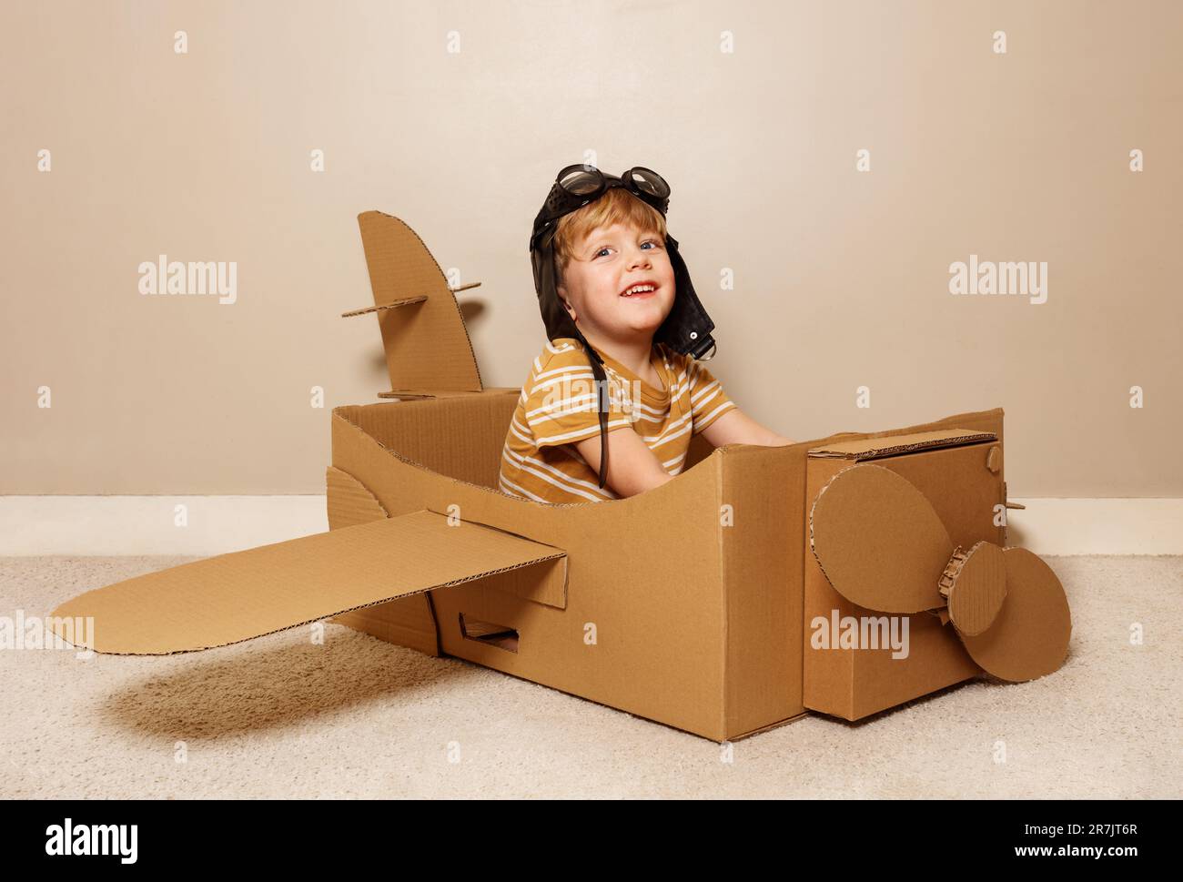 Boy sits in cardboard plane, wears hat, glasses pretends to fly Stock ...