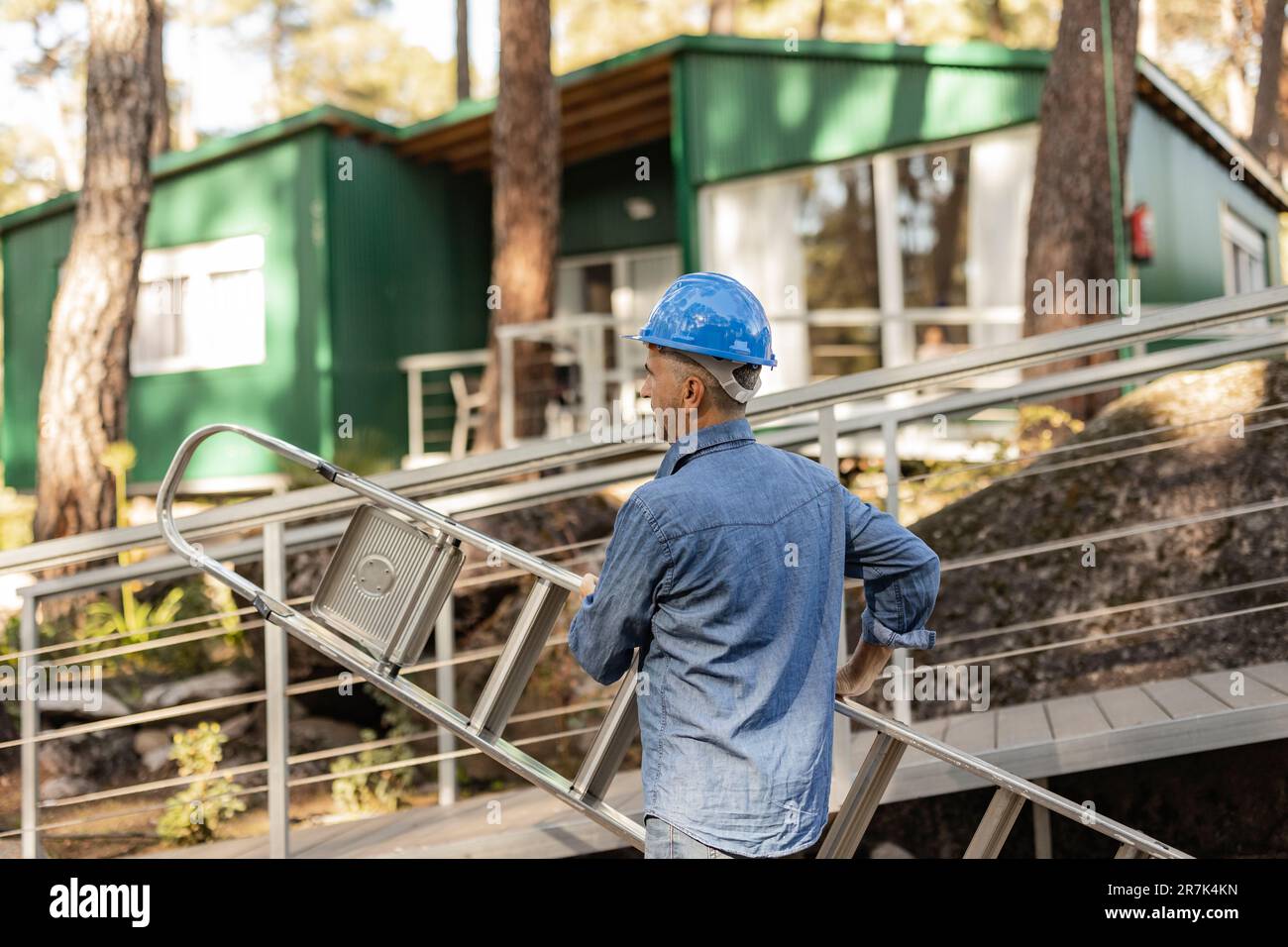 Construction worker carrying ladder wearing hard hat Stock Photo - Alamy