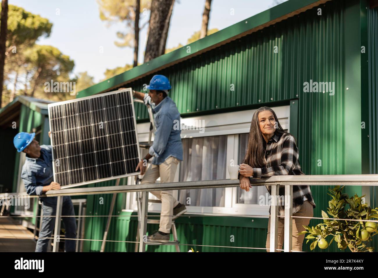 Photovoltaic technicians mounting solar panel on sustainable house with ...