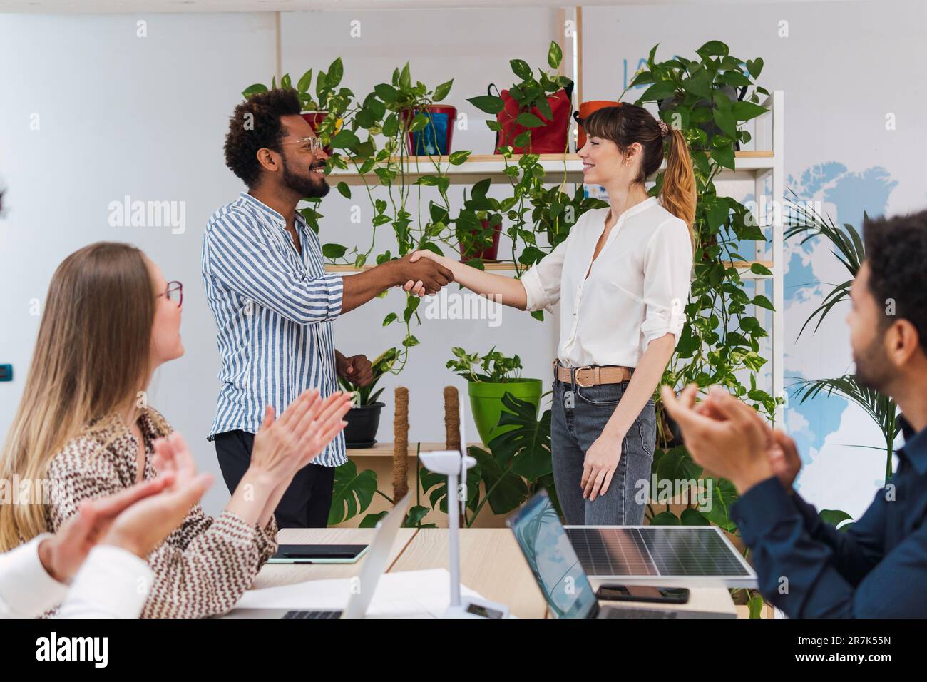 Businessman and businesswoman shaking hands in office with colleagues ...