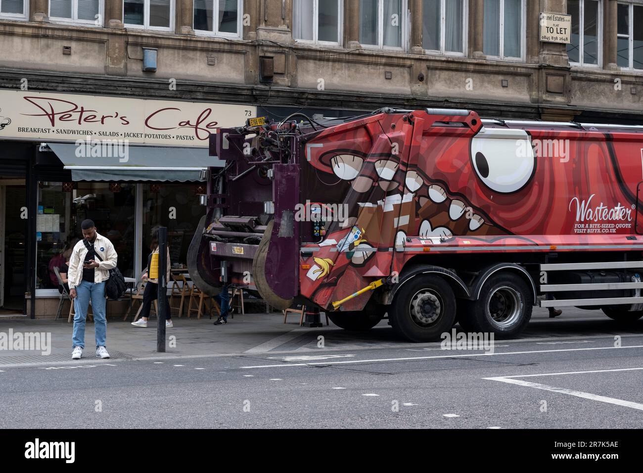 Large waste eater truck contrasts with a man looking at his phone on ...