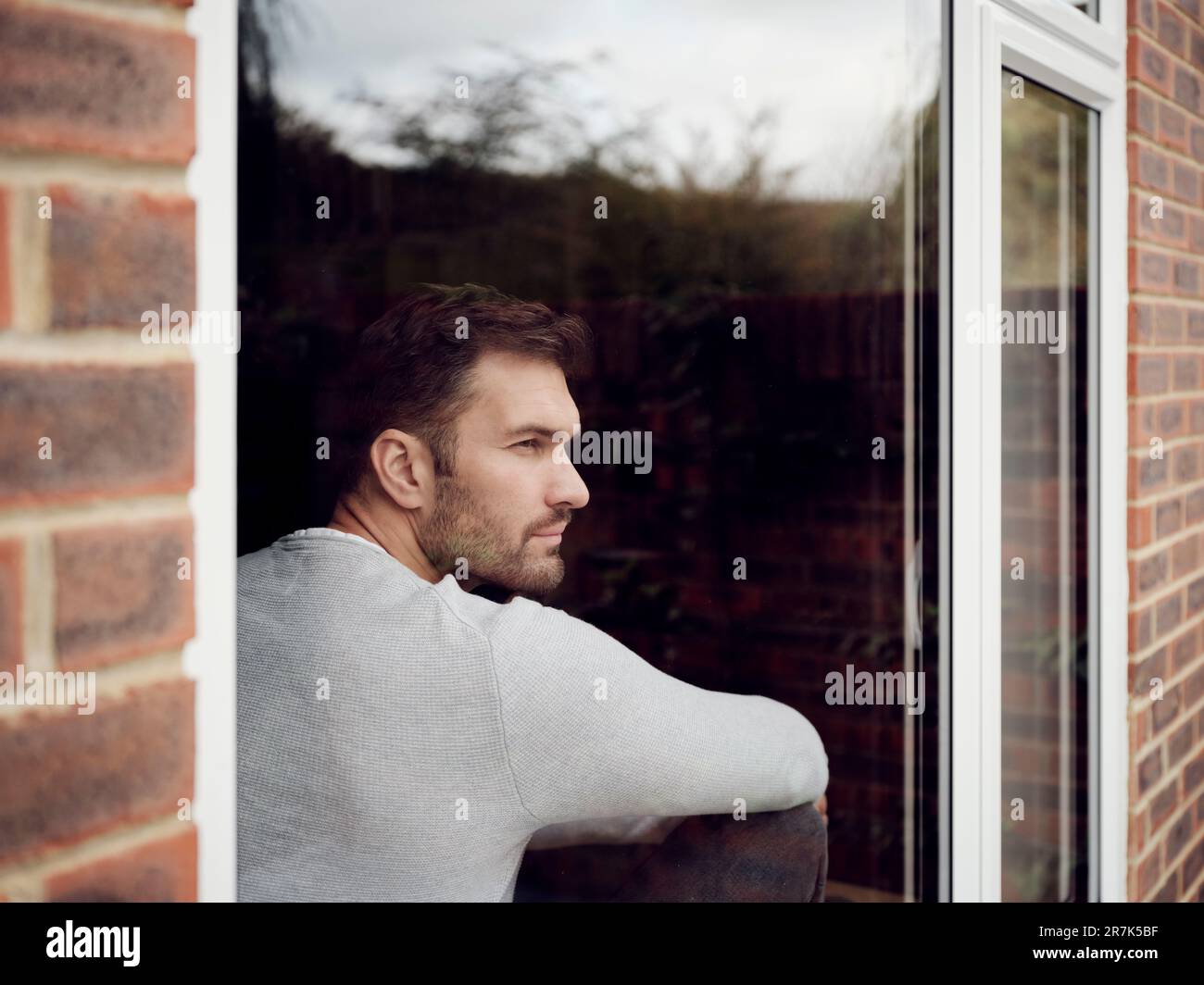 Pensive man looking out of the window at home Stock Photo - Alamy