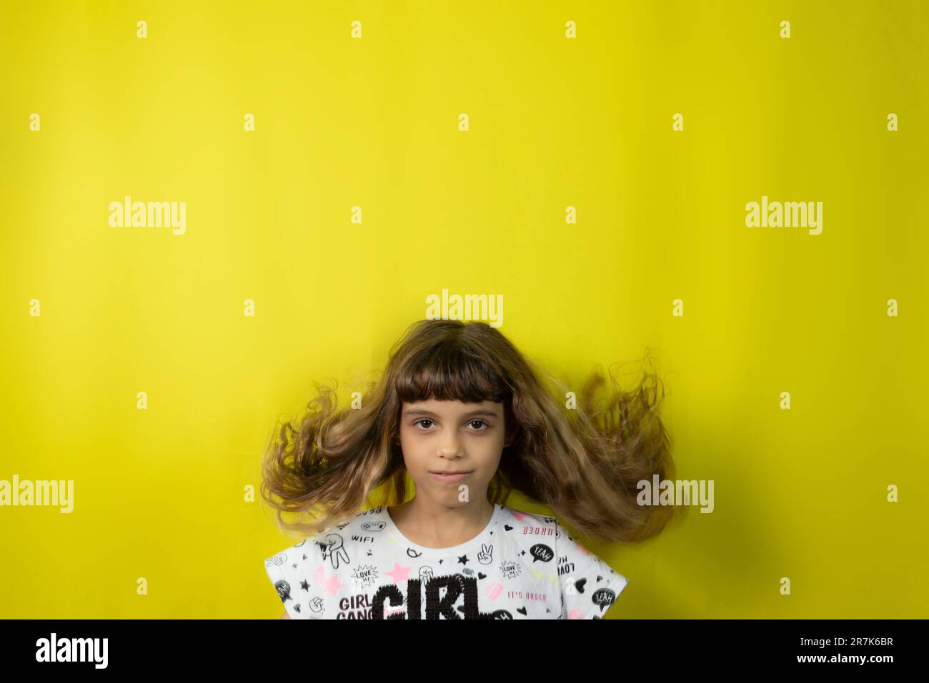 Beautiful girl throwing her long hair up. Isolated on yellow background ...