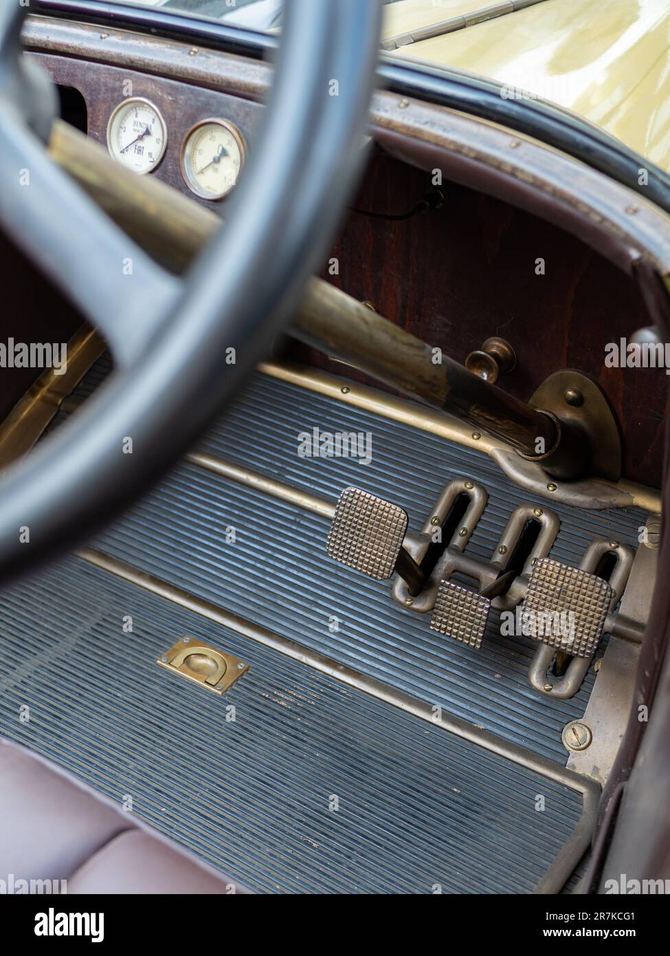 An antique-style steering wheel with three silver-colored foot pedals ...