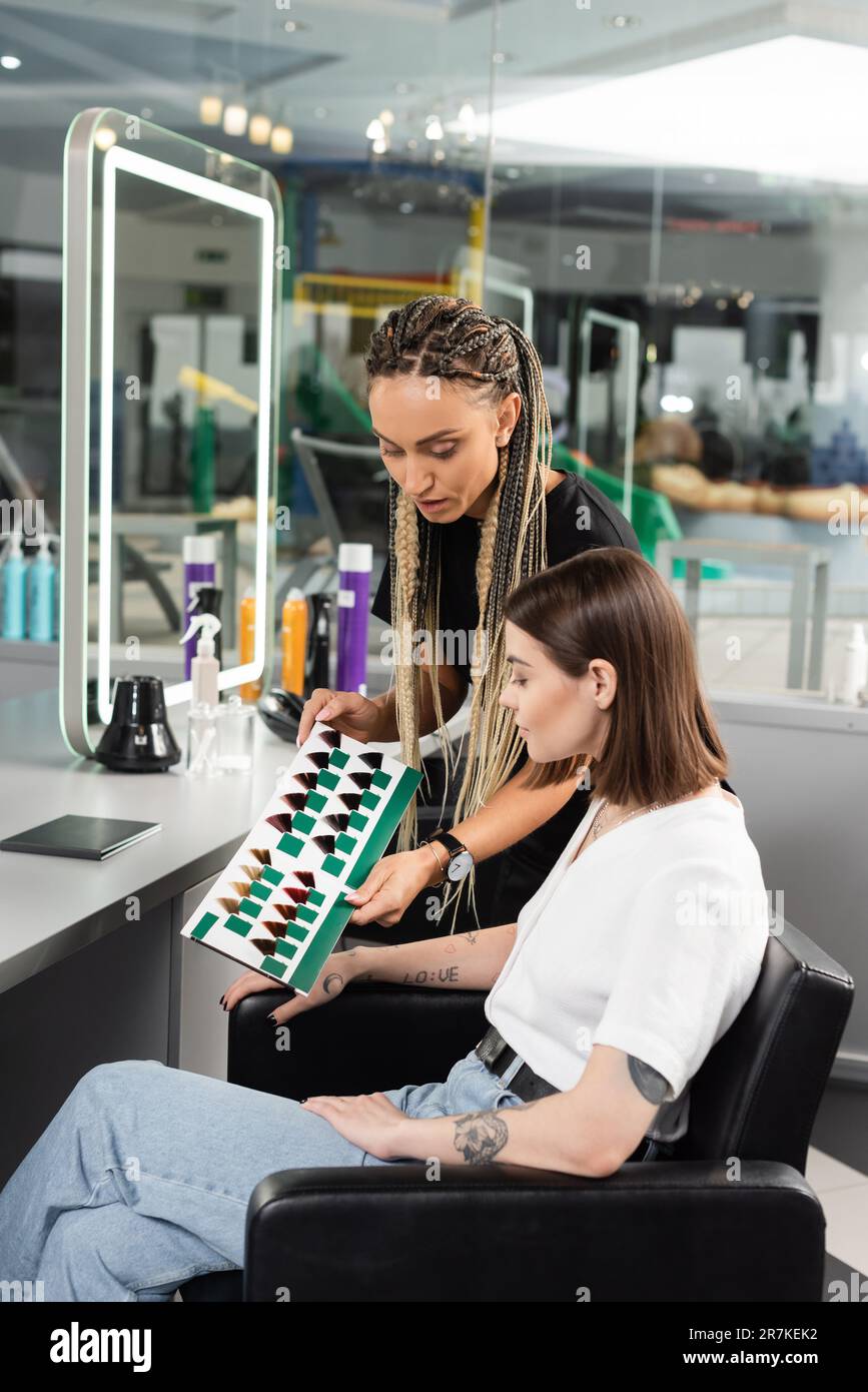 beauty worker showing hair color palette, tattooed woman choosing hair ...