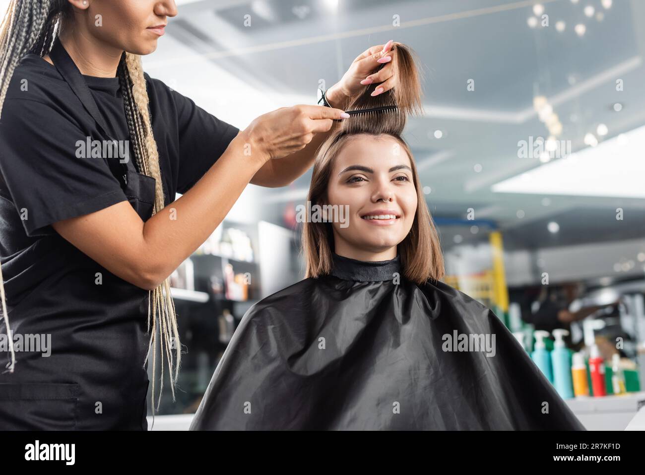 beauty profession, hairdo, hairdresser with braids brushing short ...