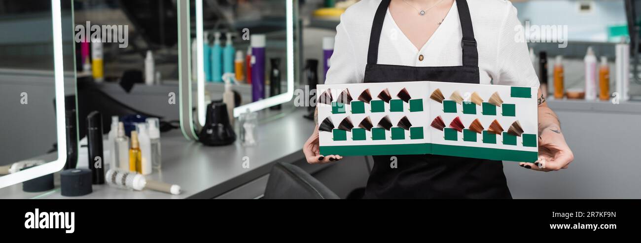hair salon, tattooed beauty worker in apron showing hair color palette ...