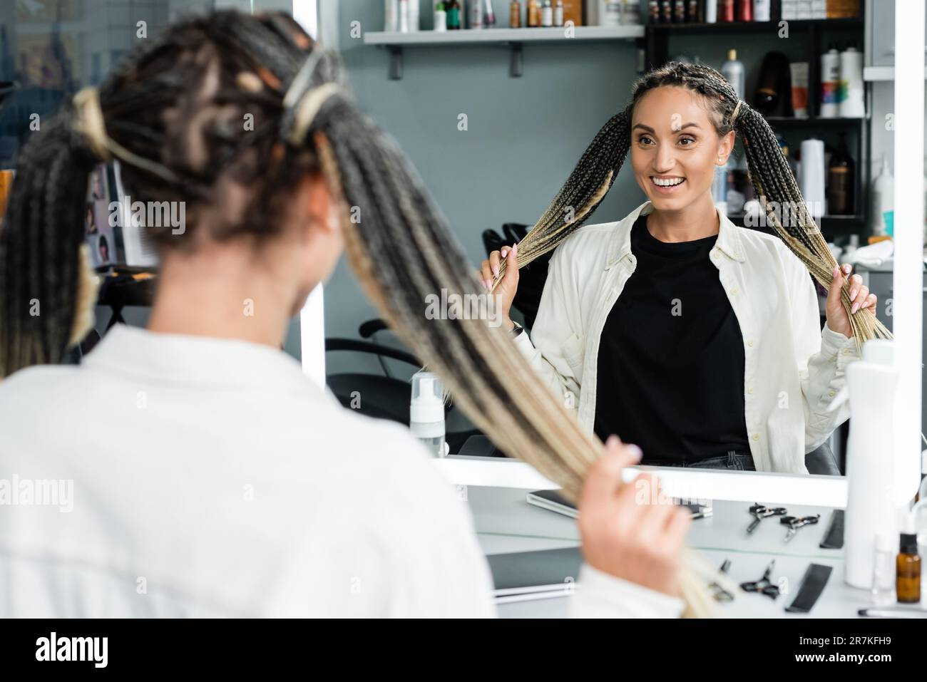 happy client in beauty salon, cheerful woman with braids looking at ...