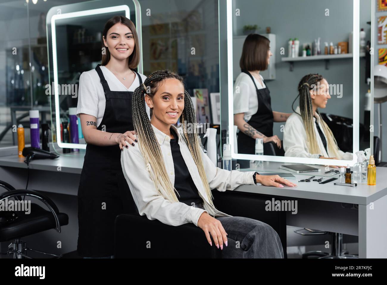 hairdresser and female client, beauty salon, cheerful woman with braids ...