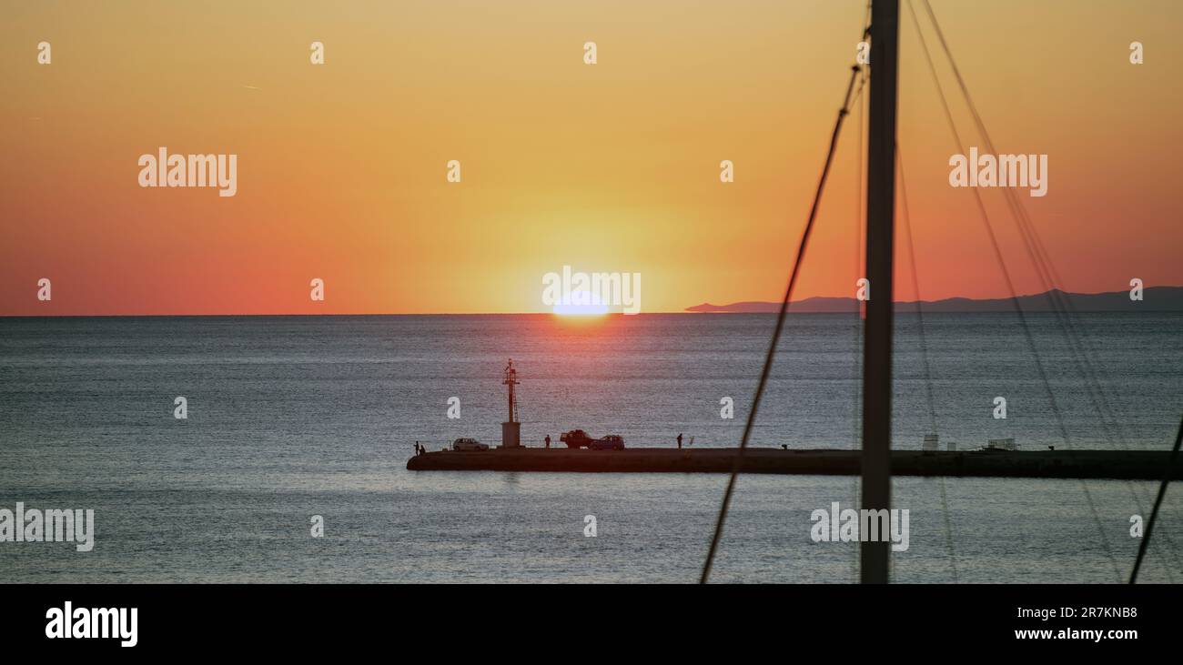Sunset over Tinos island, Cyclades, Greece. View of ship mast, beacon ...