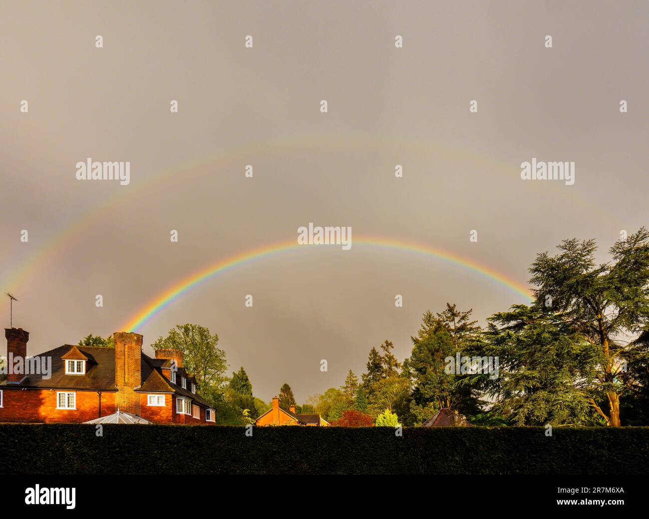 A full complete colourful double rainbow over the garden and trees of a ...