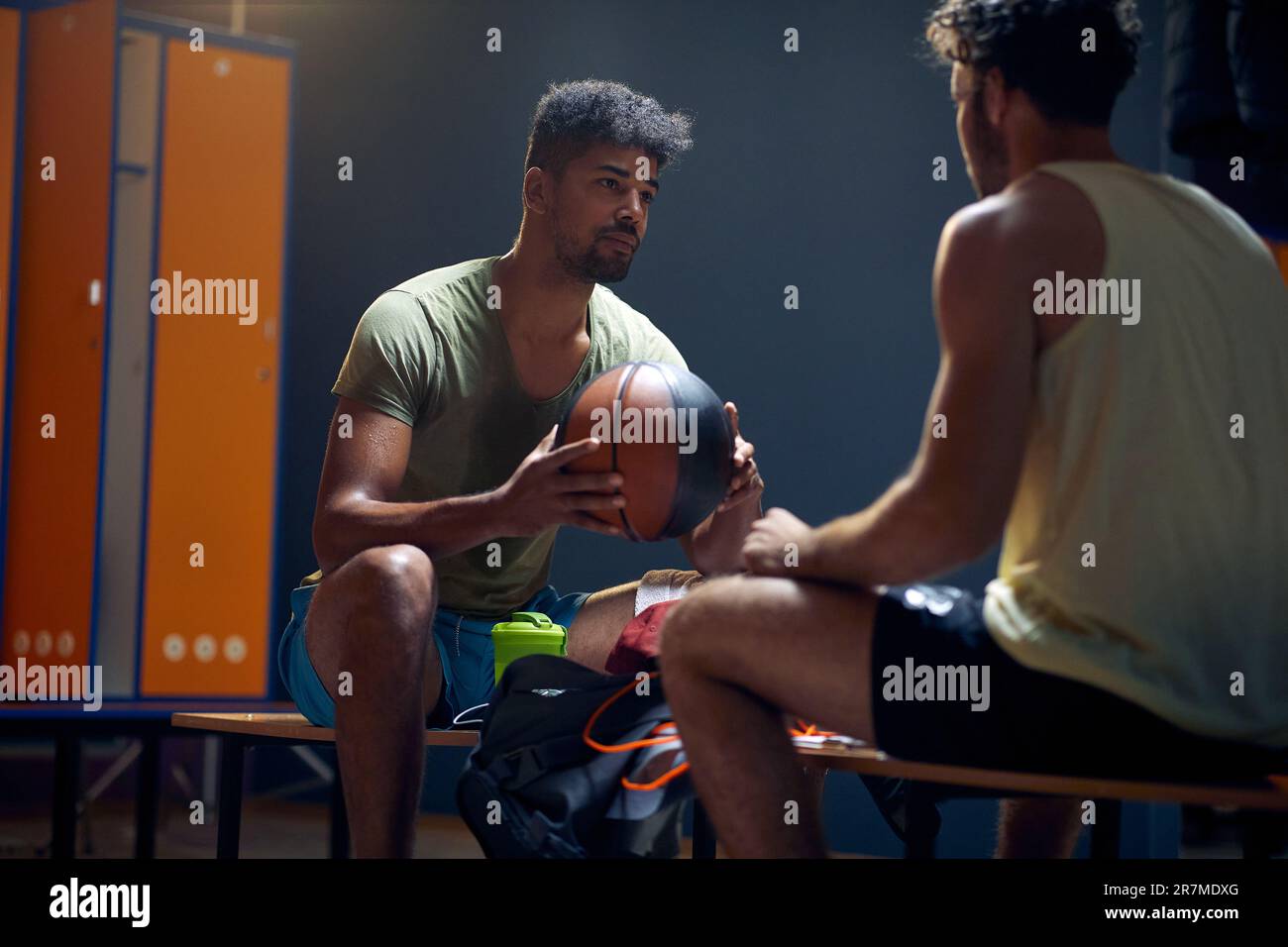Two handsome young basketball players sitting in dressing room on bench ...