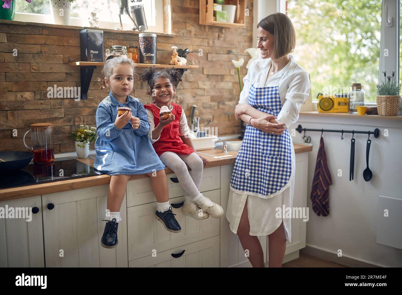 Joyful young mother together in the kitchen with two little girls ...