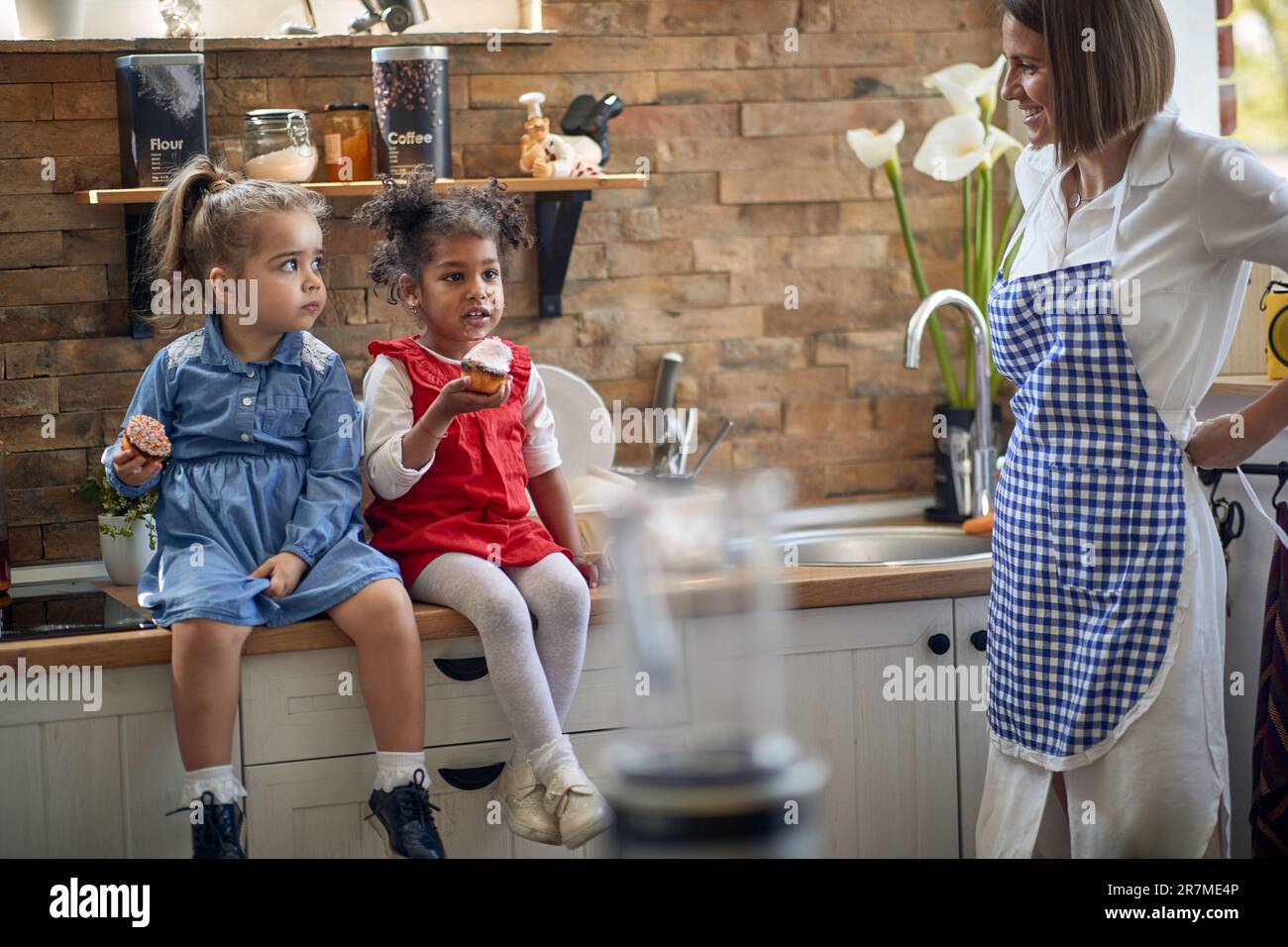 Young woman, mother looking at her daughters enjoying muffins. Two ...