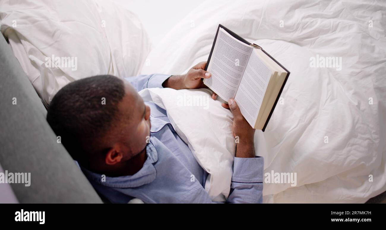 Happy Young African Man Reading His Book On Bed Stock Photo - Alamy