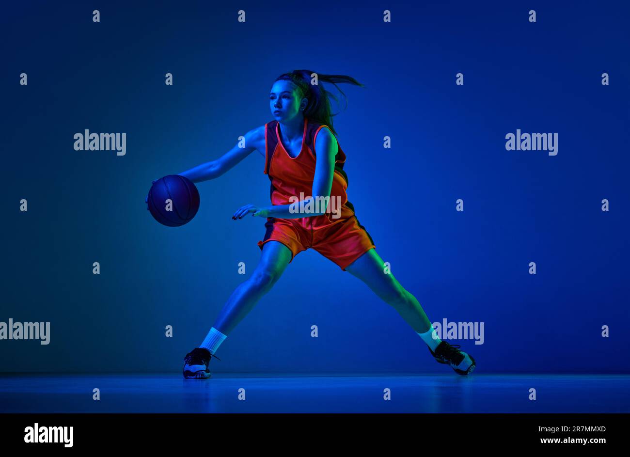 Concentrated female basketball athlete training, dribbling ball against ...