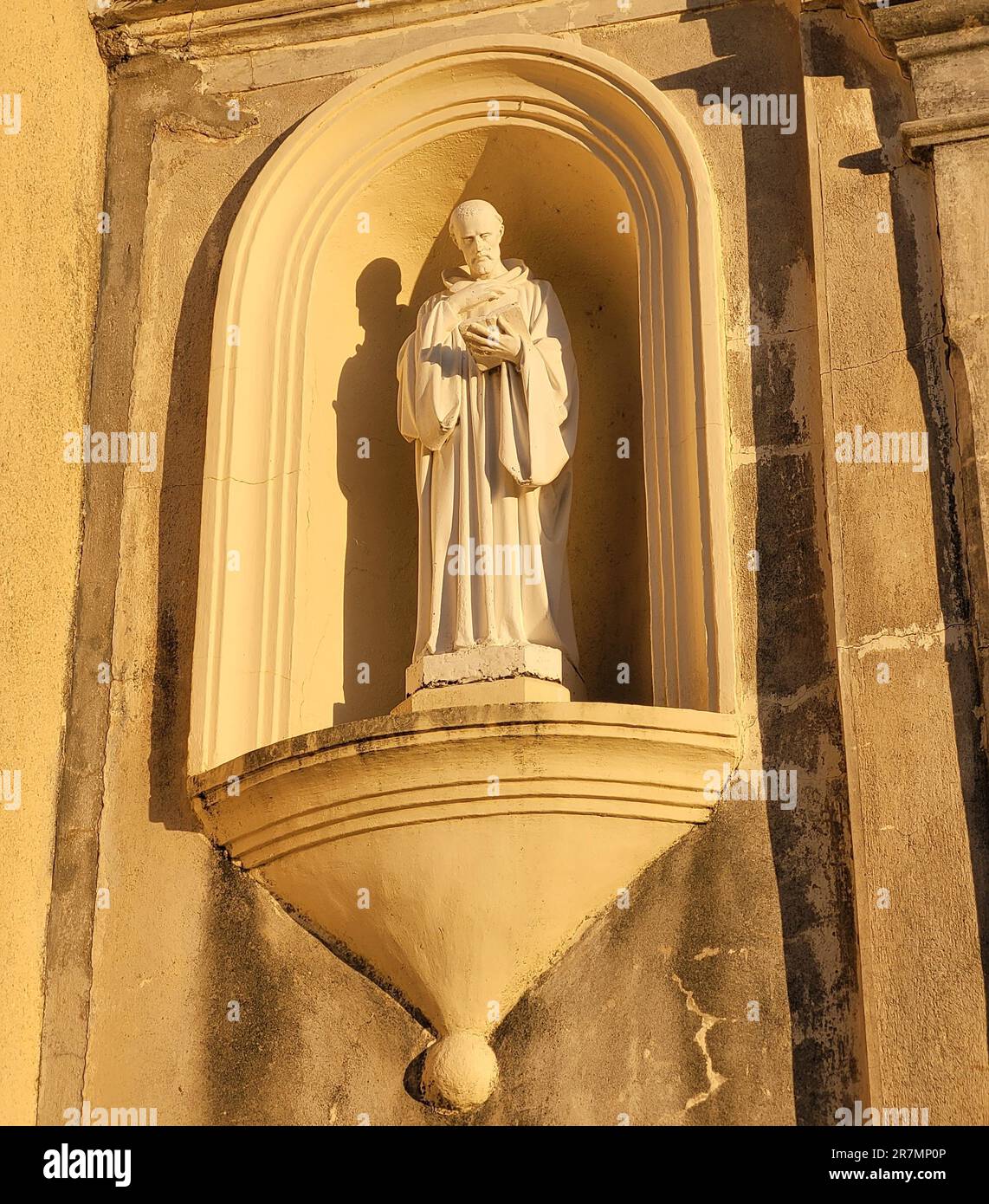 A grand stone statue of a priest standing atop a wall above a doorway ...