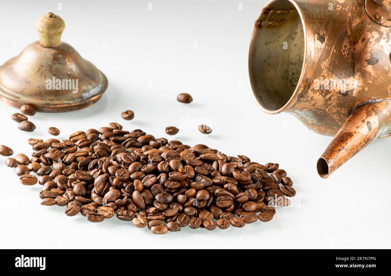 Coffee beans spilled out of an old copper coffee pot lying on its side ...