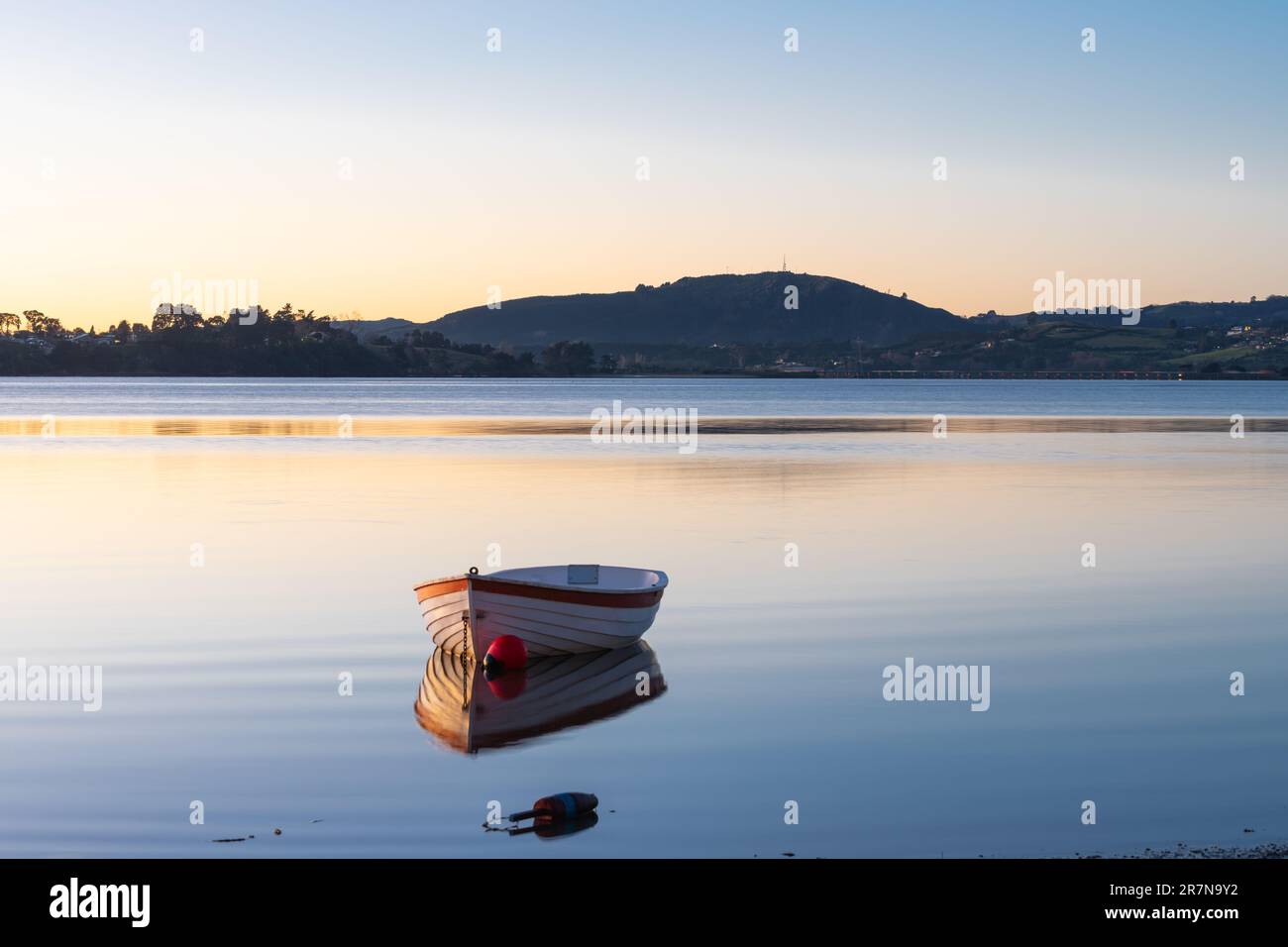 Sunrise over bay with back-lit dingy reflected in calm water Stock ...