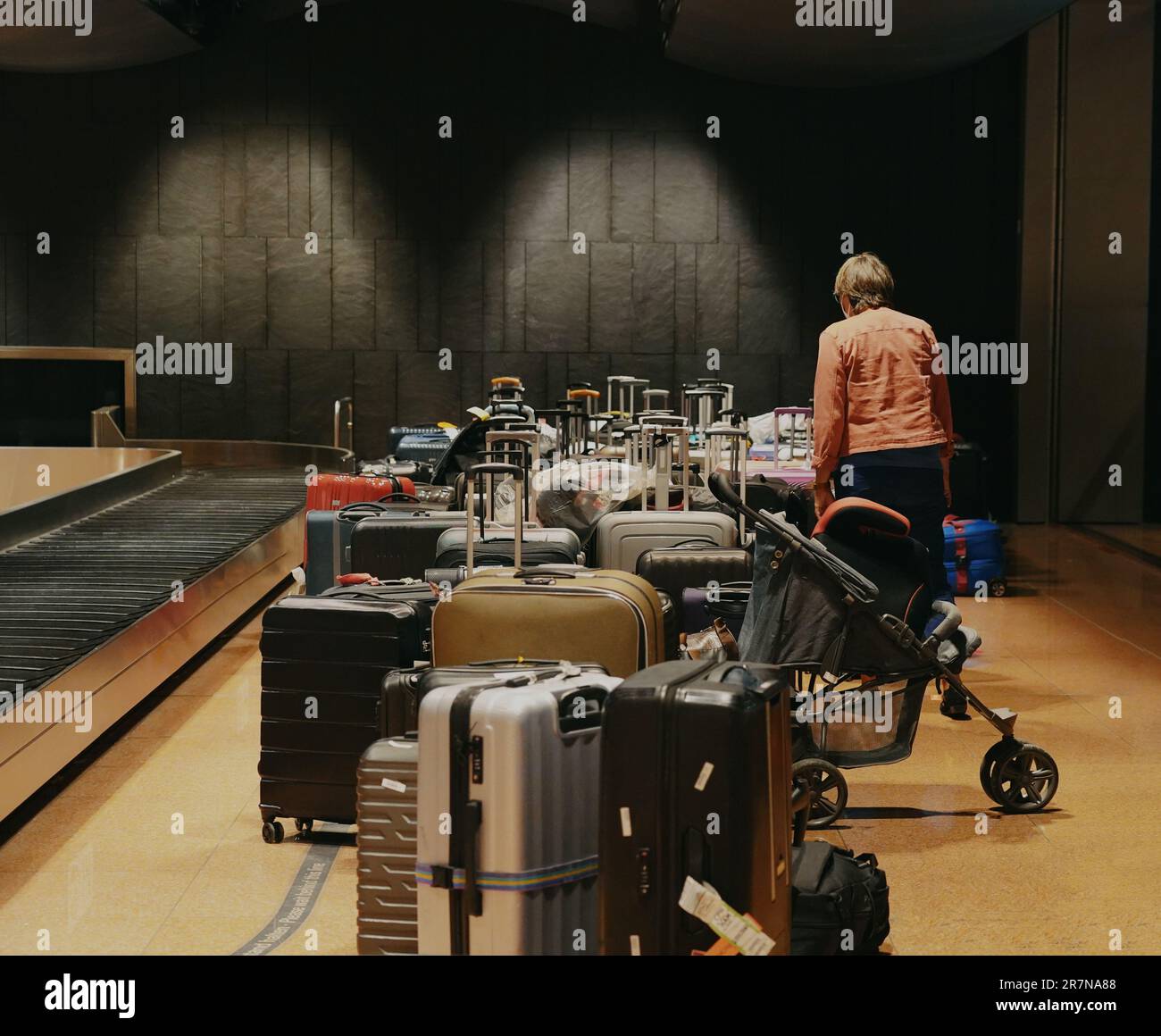 An adult man standing at a luggage carousel, looking at the suitcases ...