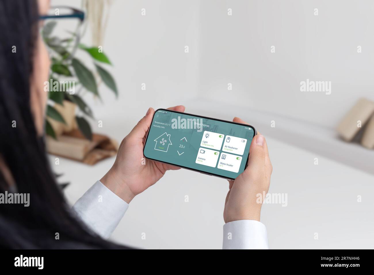 Integration of technology and home comfort concept. Woman holding a mobile phone, controlling a ...