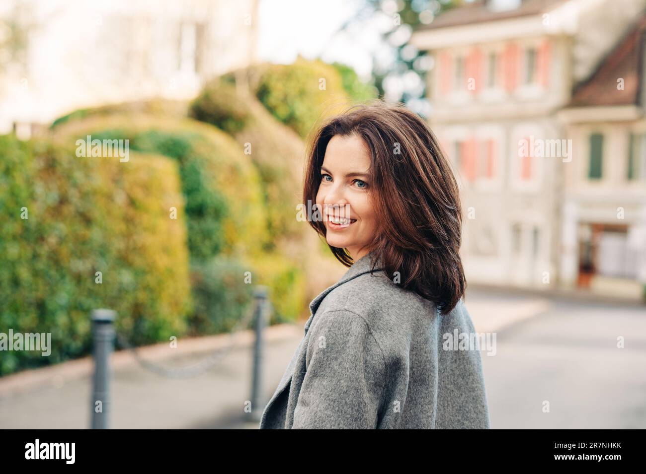 Outdoor portrait of beautiful woman wearing grey coat, smiling, looking ...