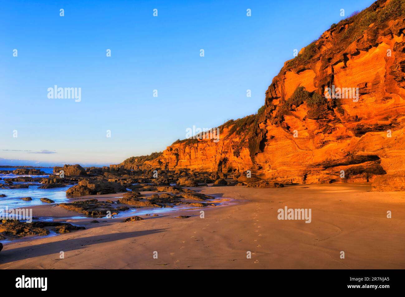 Scenic sandstone cliffs on Caves beach sand at sunrise in soft sun ...