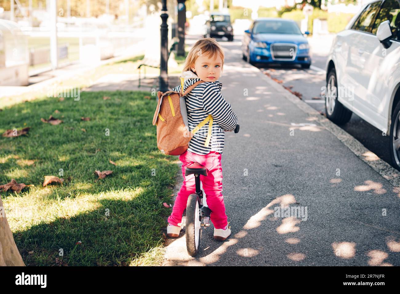 Outdoor portrait of a cute little toddler girl, riding a bike, wearing ...