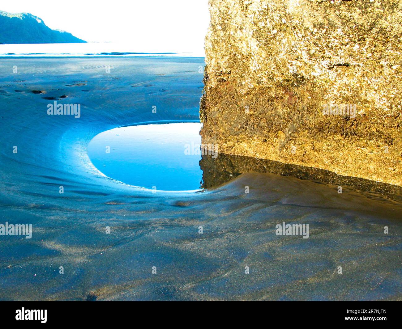 Sky reflected in a small blue puddle, black basalt sand, New Zealand ...