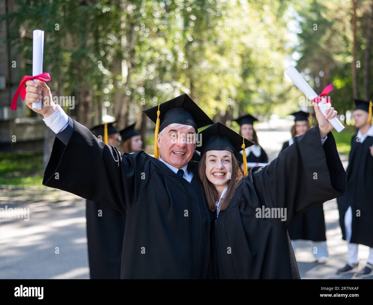 A group of graduates in robes outdoors. An elderly man and a young ...