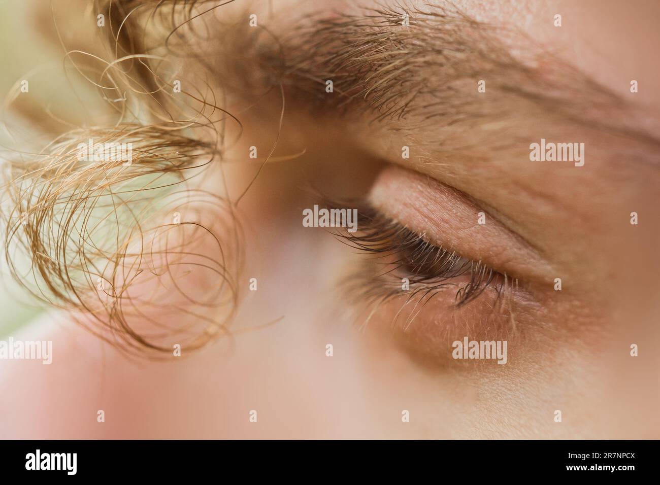 male eye close up. a curl of curly hair hangs over a man's face ...