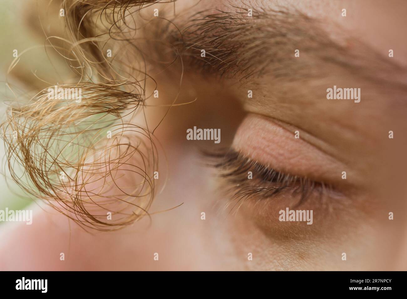 male eye close up. a curl of curly hair hangs over a man's face ...