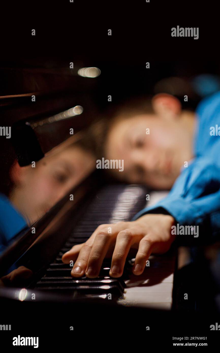 young man sitting at the piano. the boy lies on the keys and plays the ...