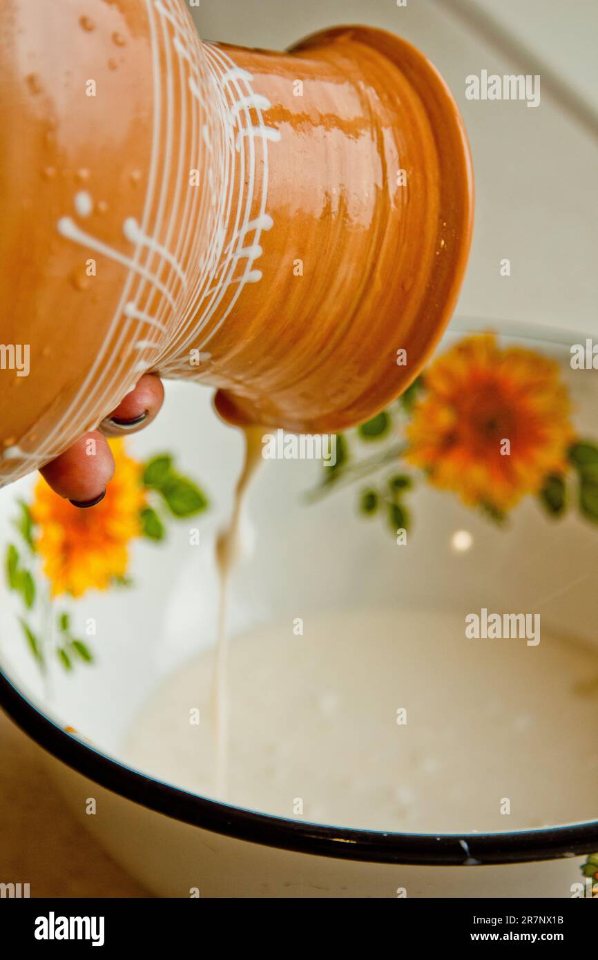 female hand pouring milk from ceramic ewer into a metal bowl. painted ...