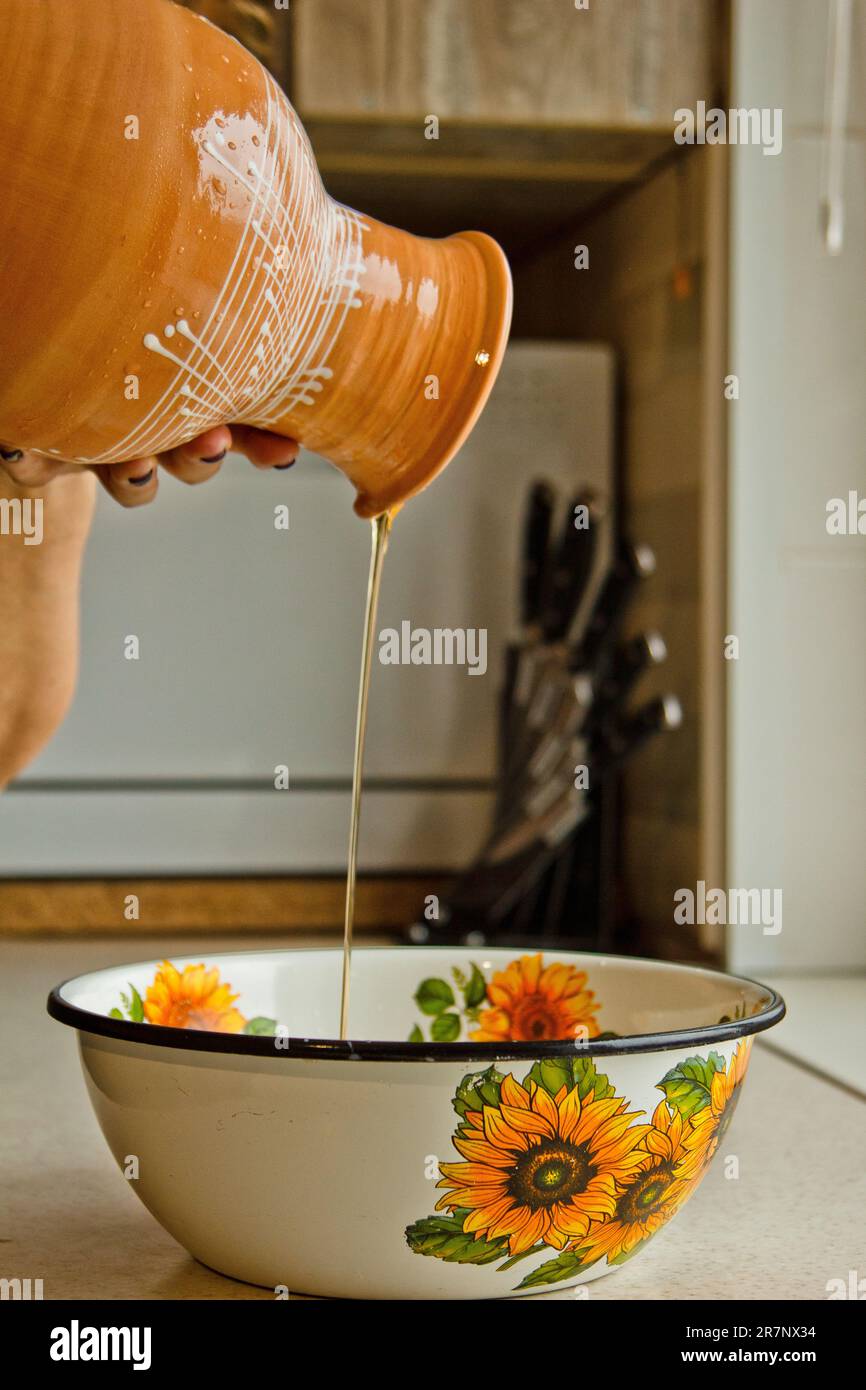 female hand pouring ceramic ewer oil into a metal bowl. painted in ...
