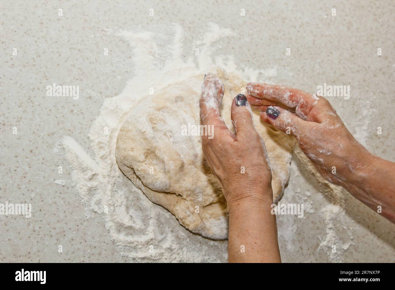 Female hands knead the dough with flour on a white kitchen table. Top ...