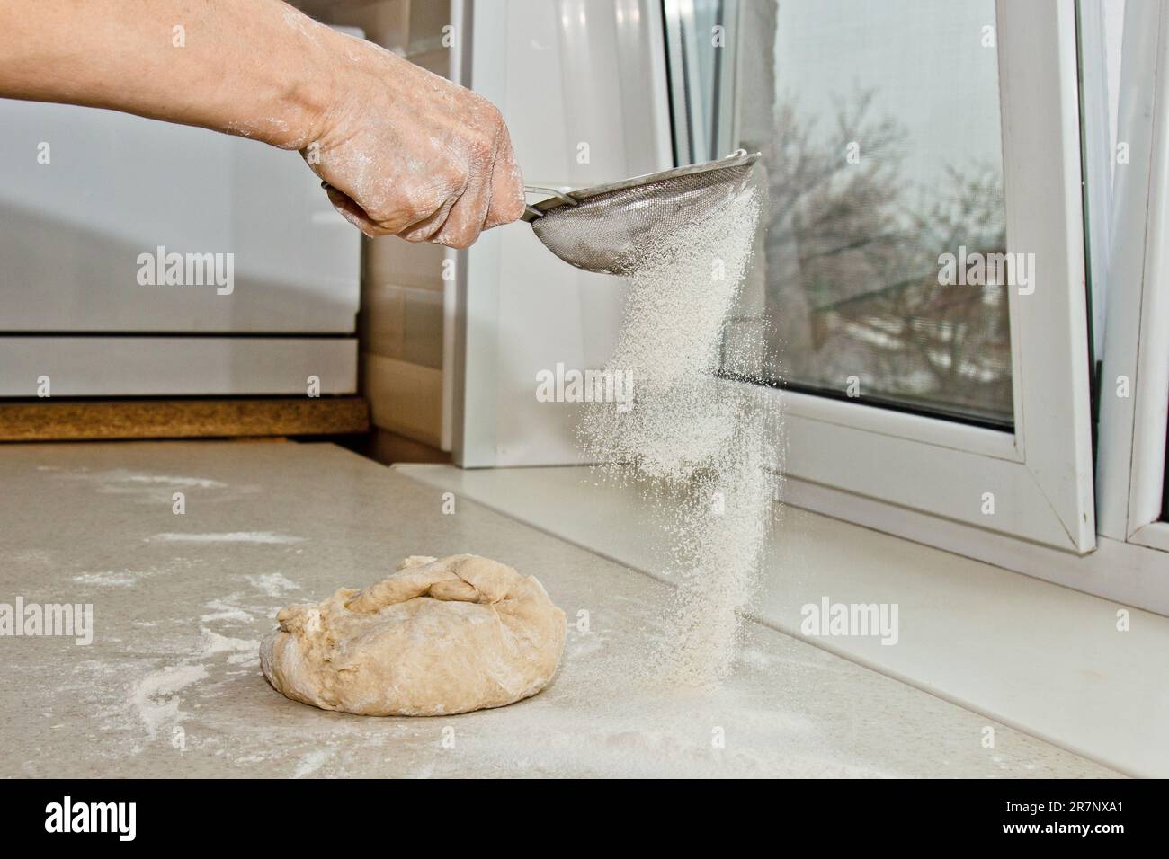 female hand sifting flour through manual flour sieve in a bowl close-up ...