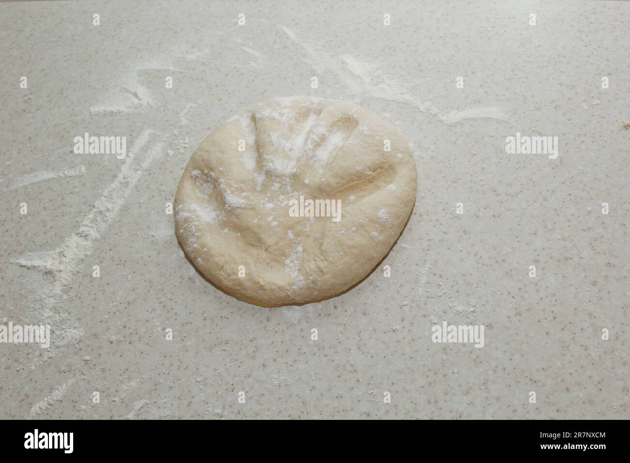 A pile of kneaded dough sprinkled with wheat flour is lying on a white ...