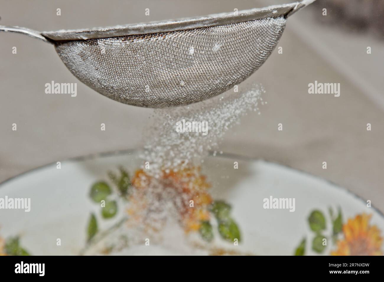 female hand sifting flour through manual flour sieve in a bowl close-up ...