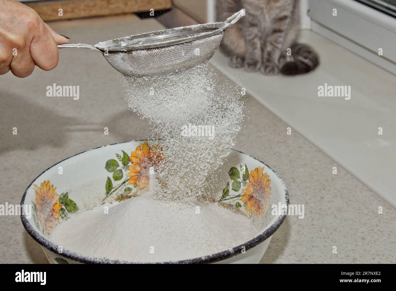 female hand sifting flour through manual flour sieve in a bowl close-up ...