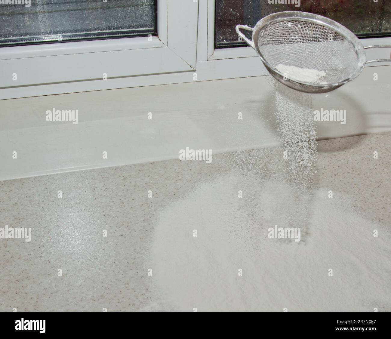 female hand sifting flour through a hand sieve for flour on a white ...