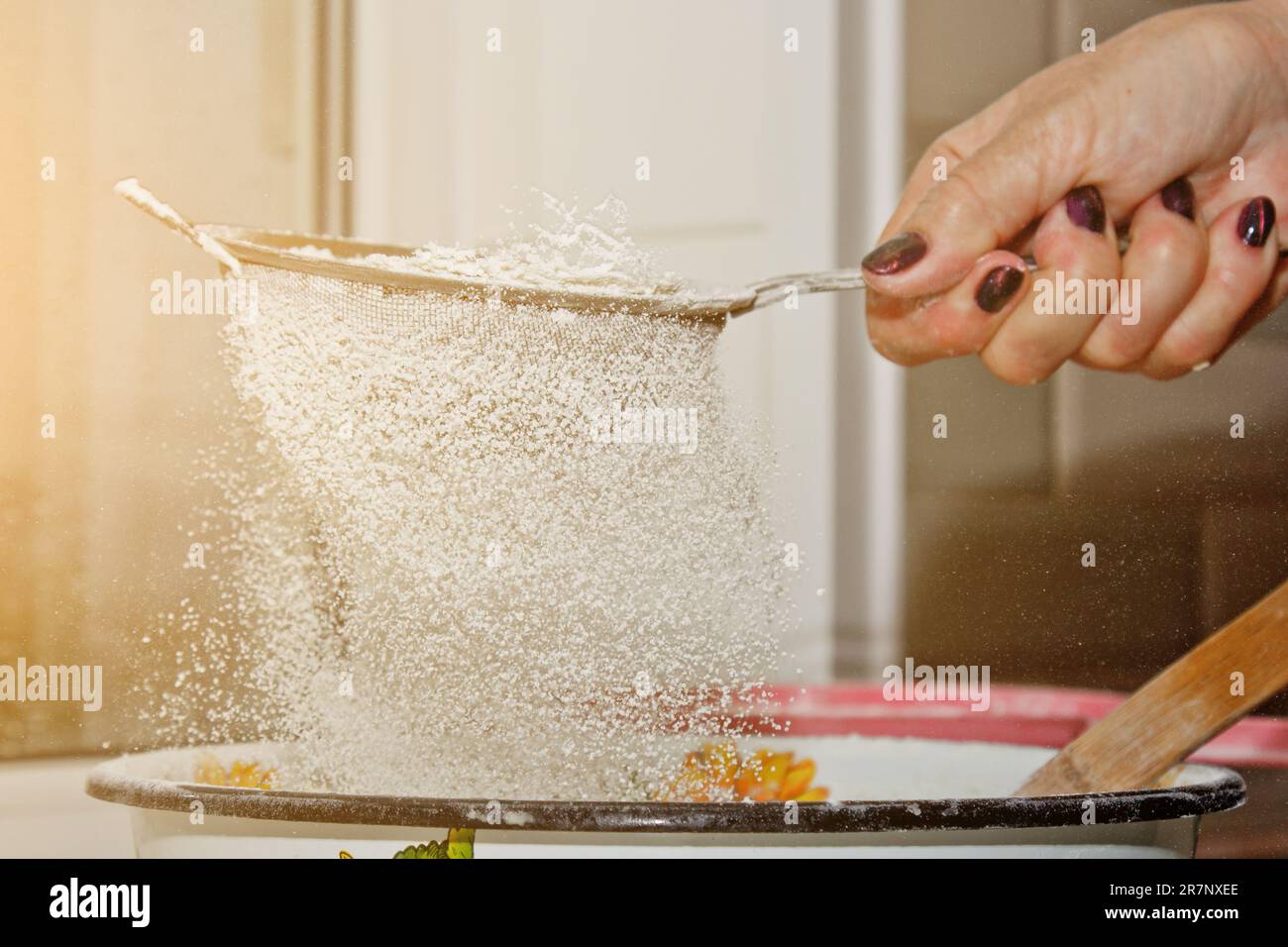 female hand sifting flour through manual flour sieve in a bowl close-up ...