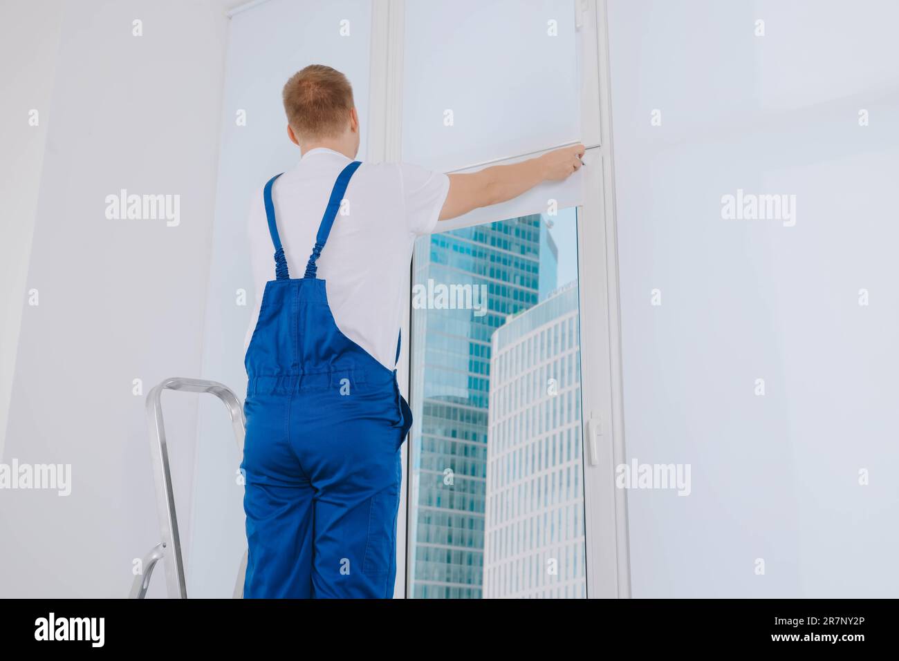 Worker installing roller window blind on stepladder indoors Stock Photo ...