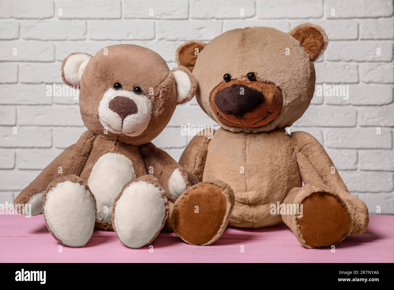 Cute teddy bears on pink wooden table near white brick wall Stock Photo ...