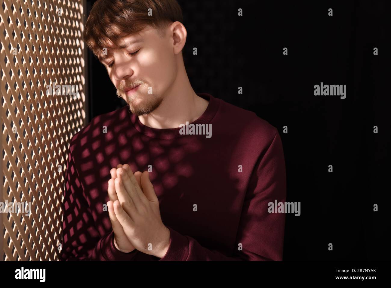 Man praying during confession near wooden window in booth. Space for ...