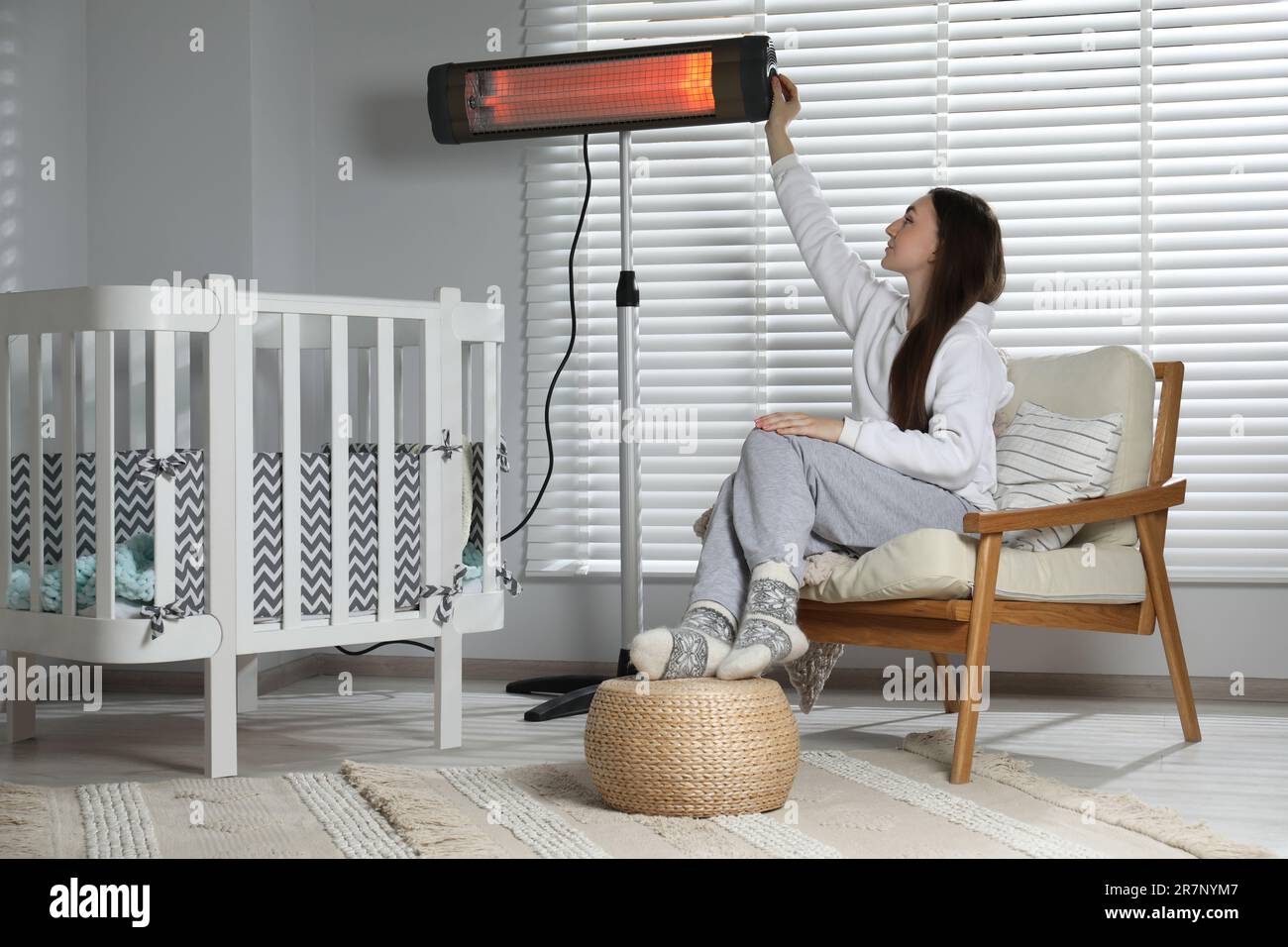 Young woman adjusting temperature on modern electric infrared heater in ...