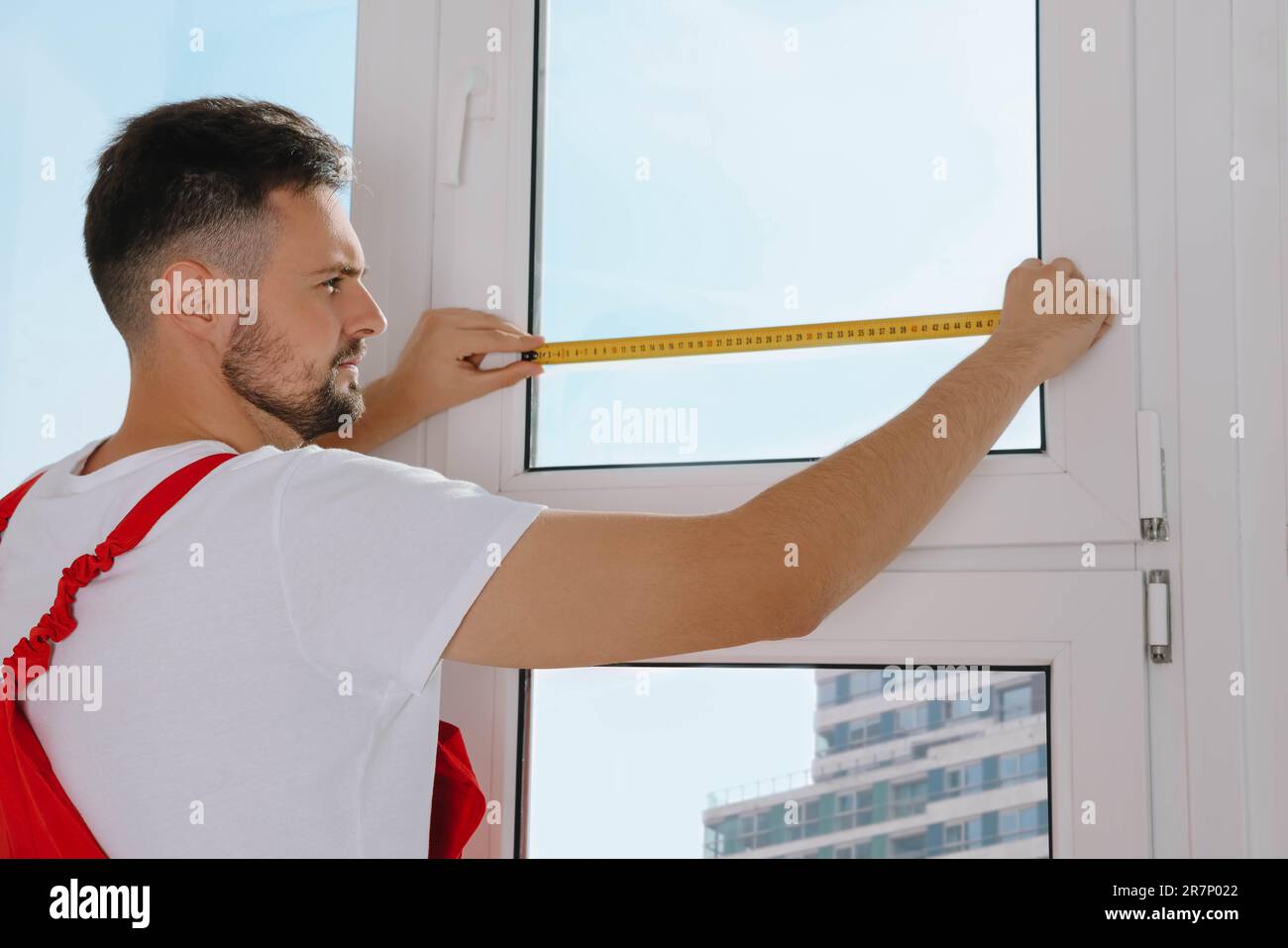 Worker in uniform measuring window with tape indoors. Roller blinds ...