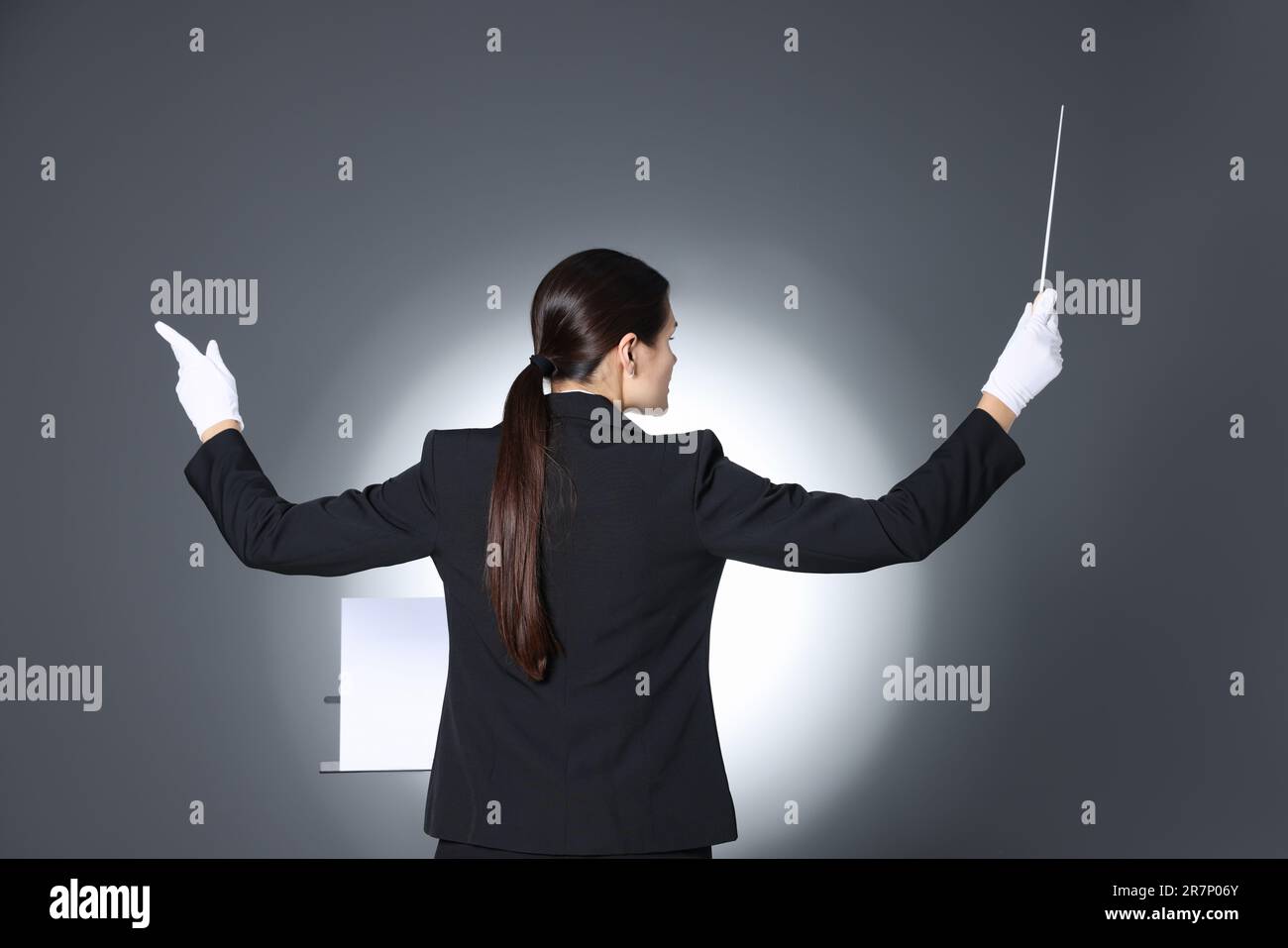 Professional conductor with baton and note stand on grey background ...