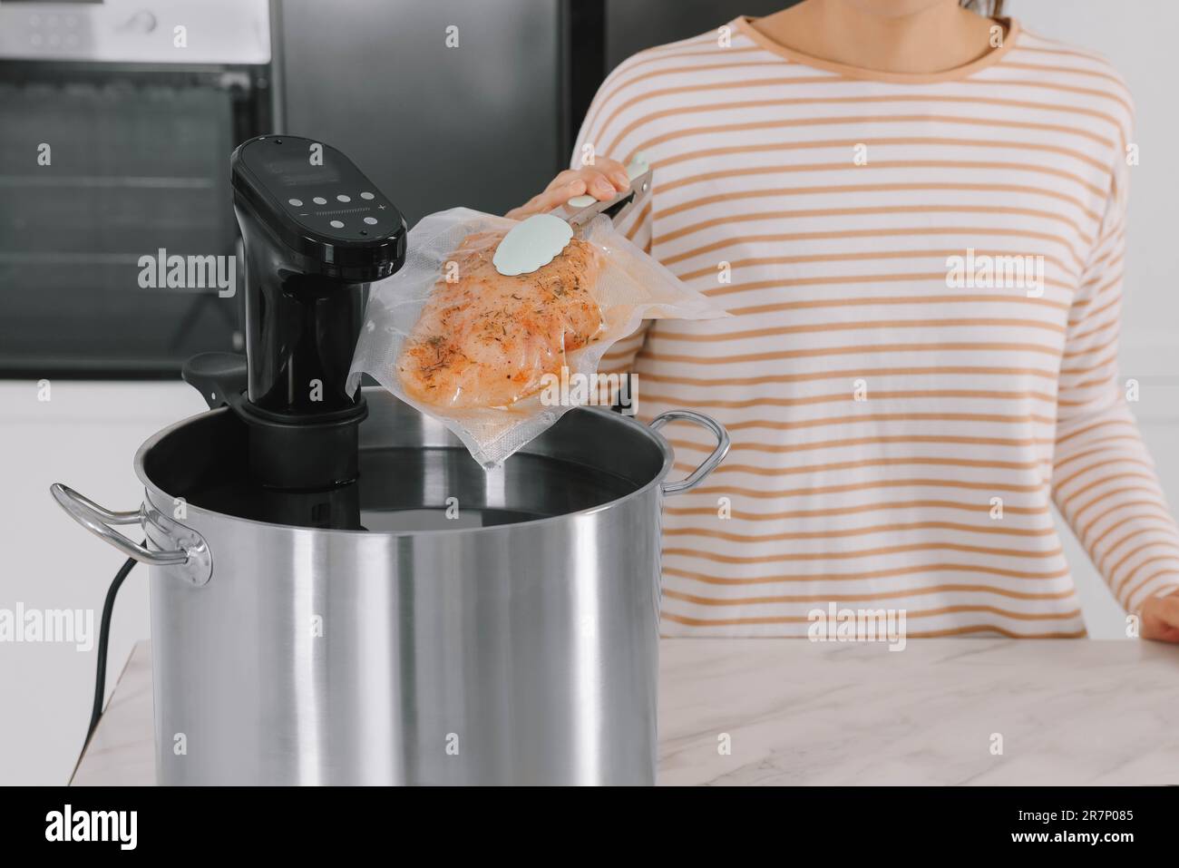 Woman putting vacuum packed meat into pot with sous vide cooker in ...