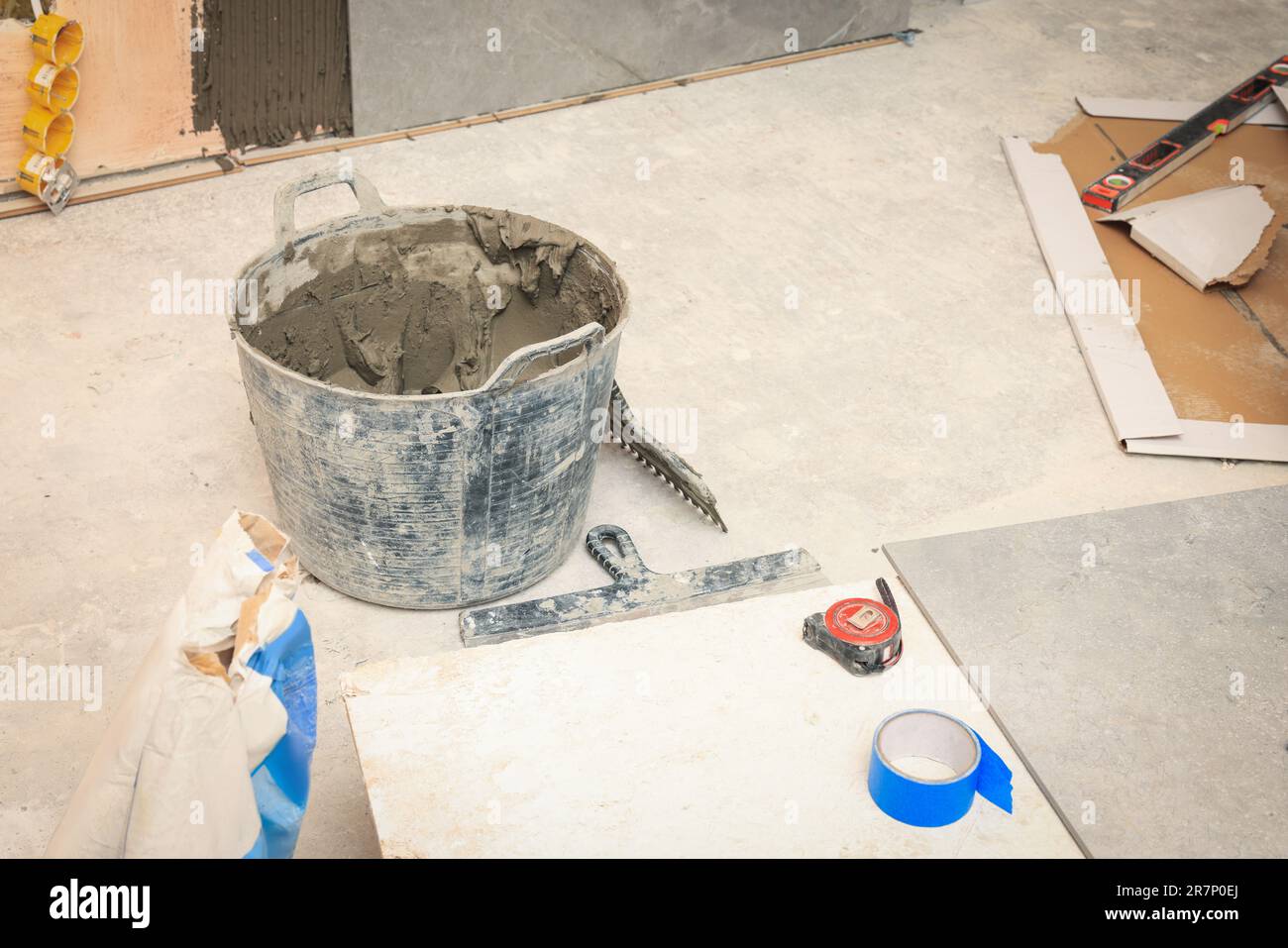 Bucket of adhesive mix and different tools on floor indoors. Tile ...